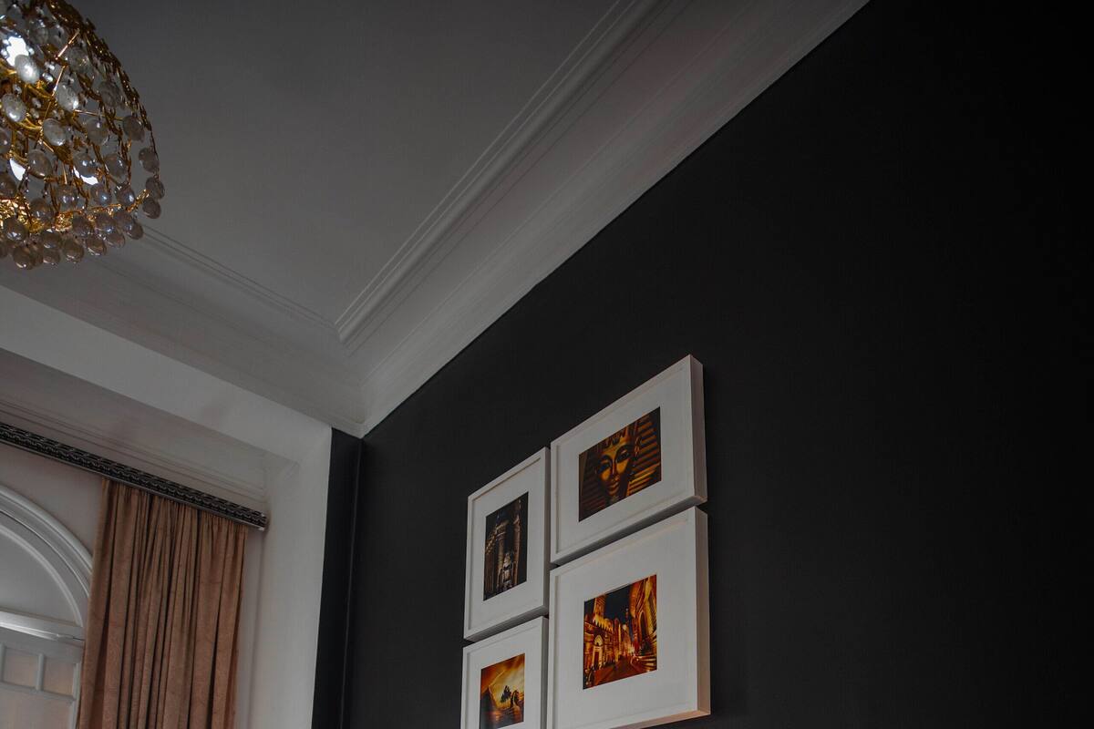 Cama bem arrumada com lençóis brancos, cabeceira estofada e luminária ao lado. Há quadros na parede acima da cama.