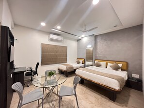 Quarto de hotel moderno com cama, mesas de cabeceira, escrivaninha, mesa de vidro com cadeiras e um ventilador de teto.