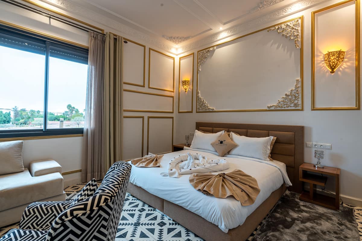 Quarto de hotel com uma cama grande, um sofá, uma mesinha e uma janela com cortinas.