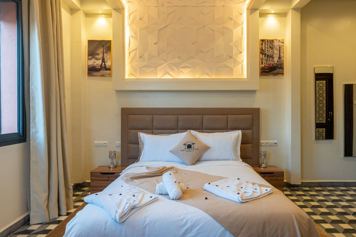 Quarto de hotel com cama grande, cabeceira, duas mesas de cabeceira e design geométrico na parede.