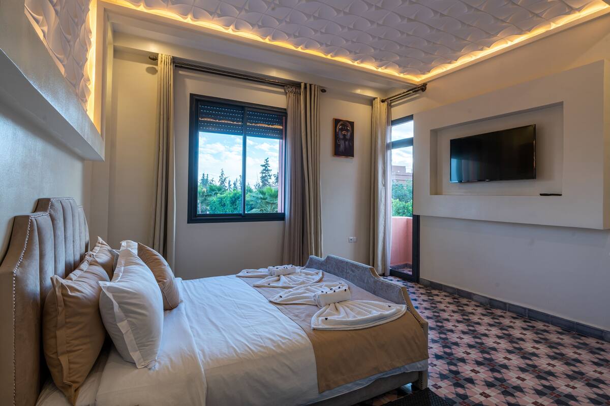 Quarto de hotel com uma cama, uma TV fixada na parede e uma janela com cortinas.