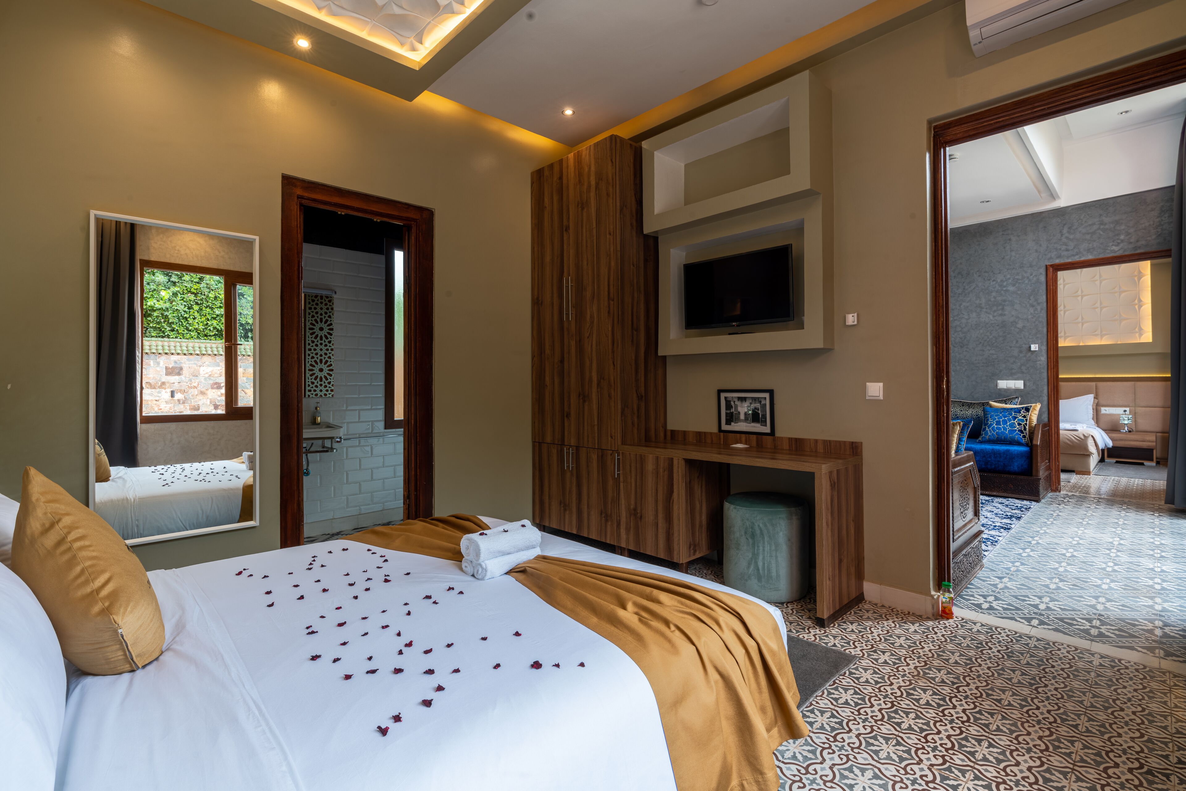 Quarto de hotel com uma cama, televisão, escrivaninha e banheiro visível através de uma porta aberta.