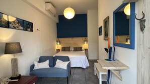 Quarto de hotel compacto com cama, sofá, pequena escrivaninha e espelho.