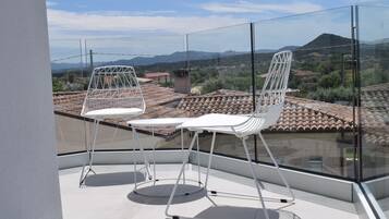 Varanda com duas cadeiras brancas e uma mesa, com vista para uma paisagem montanhosa.