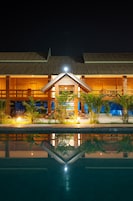 Um edifício com piscina refletora na frente, fachada de madeira e área de estar ao ar livre coberta.