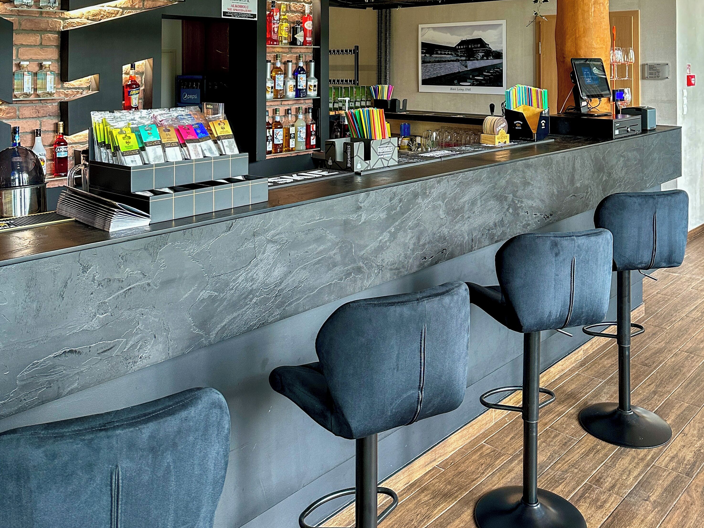 Uma área de bar com bancada de mármore, banquetas e diversos copos e garrafas.