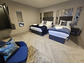 Quarto de hotel com duas camas, um sofá, um espelho e obras de arte nas paredes.