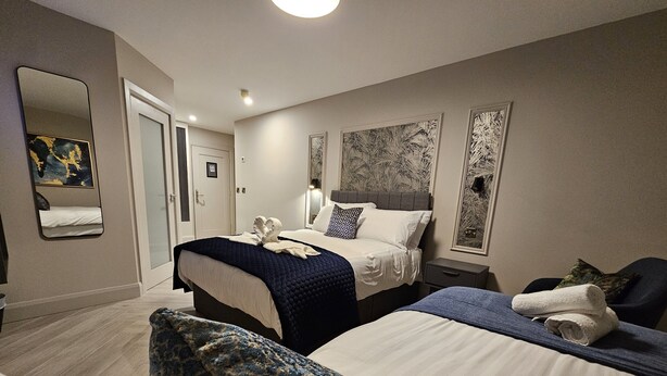 Quarto de hotel moderno com uma cama grande, uma cama menor, uma área de estar e um banheiro.