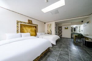 Quarto de hotel com duas camas, uma escrivaninha e uma cadeira. Possui uma janela grande e uma porta que dá para o banheiro.