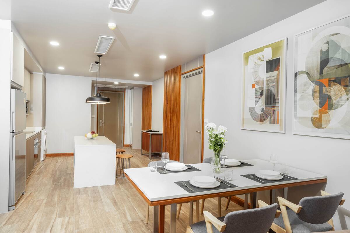 Uma cozinha moderna com uma ilha central, armários de madeira e um espaço de jantar com mesa e cadeiras brancas.