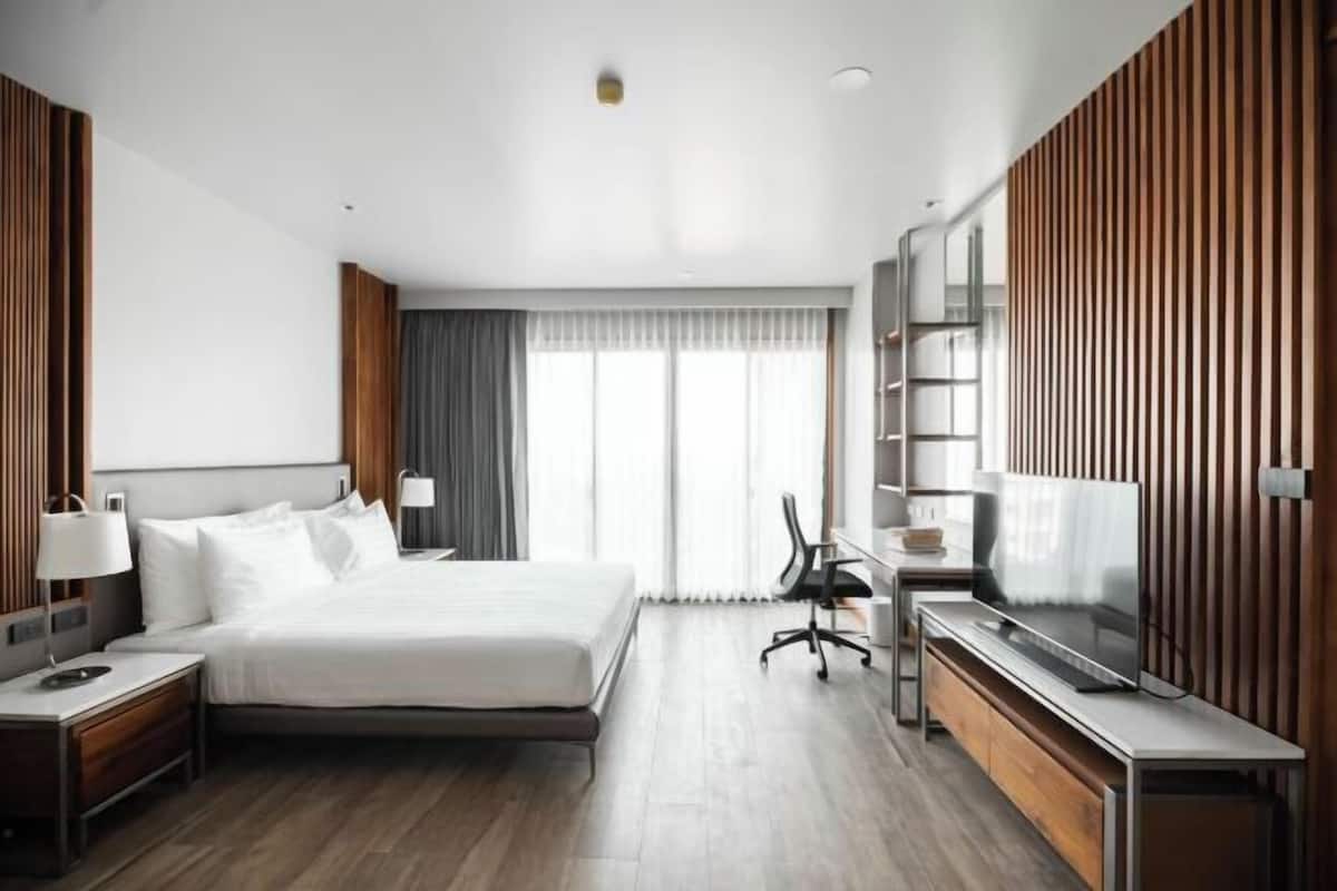 Quarto de hotel com uma cama grande, uma escrivaninha com cadeira, televisão e guarda-roupa.