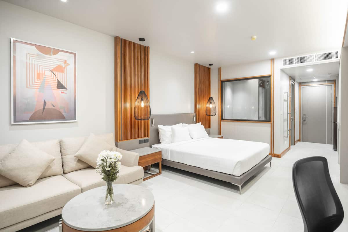 Quarto de hotel moderno com uma cama, um sofá, uma mesinha com um vaso e um espelho.