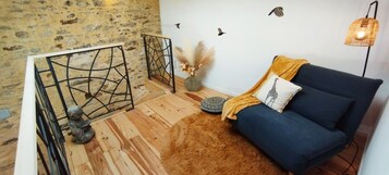 Uma sala de estar aconchegante com um sofá azul, um portão de metal decorativo, piso de madeira e parede de pedra.