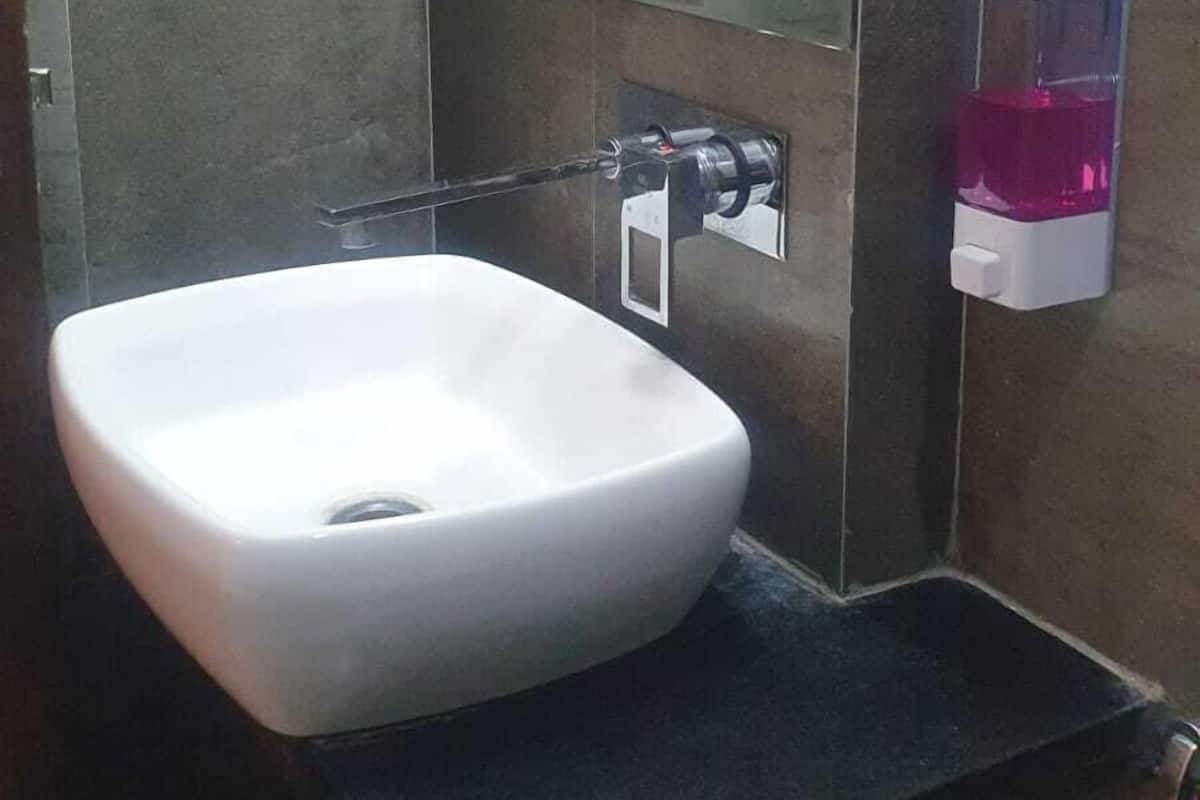 Casa de banho com uma pia branca, bancada preta e dispensador de sabão na parede.