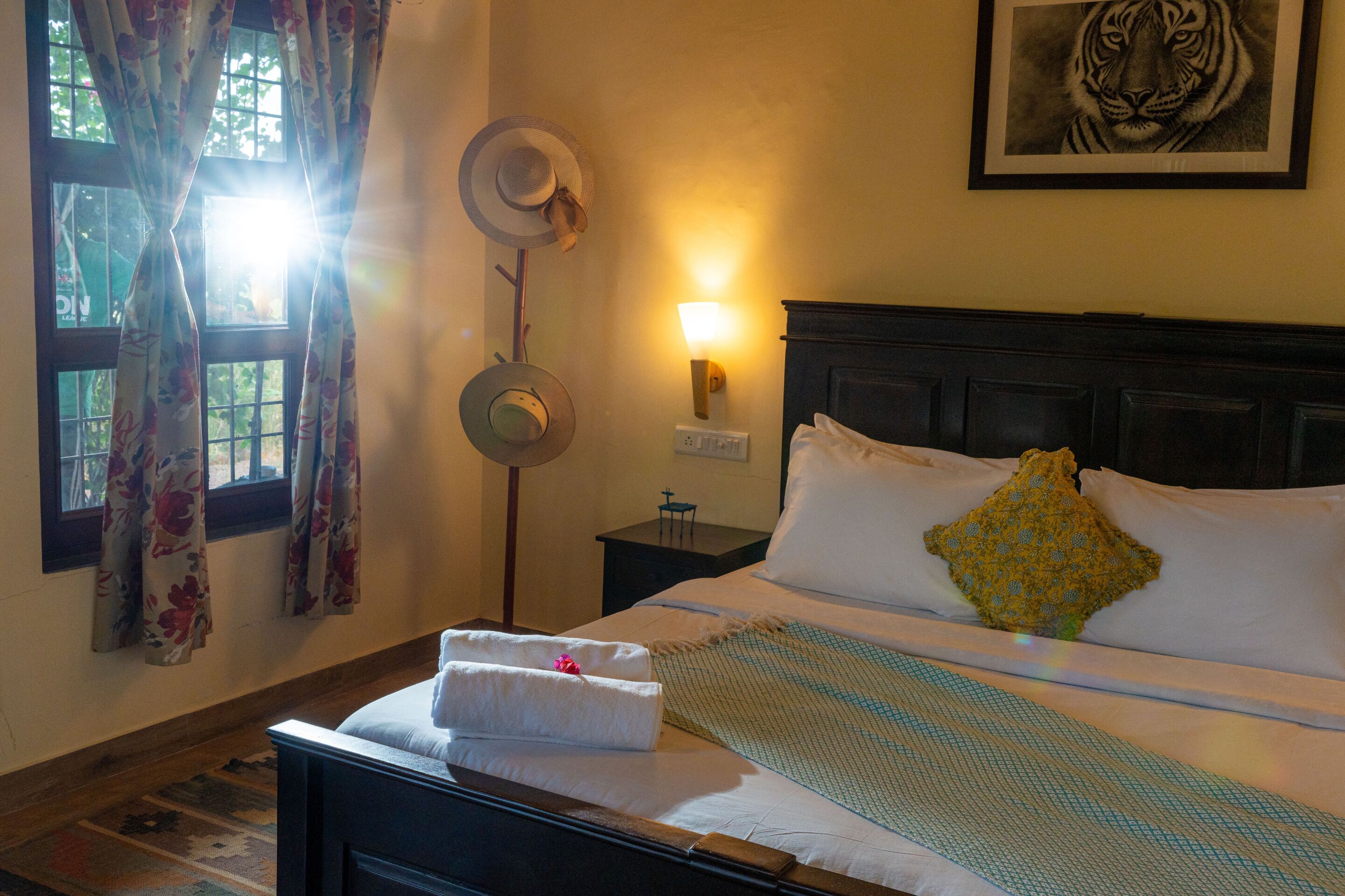 Cama bem arrumada com colcha estampada em flor, almofada decorativa e toalha no criado-mudo.