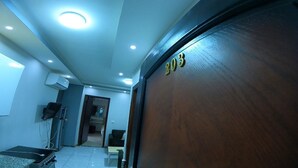 Quarto de hotel com porta de madeira marcada com o número 203, teto com iluminação embutida e ar condicionado visível.