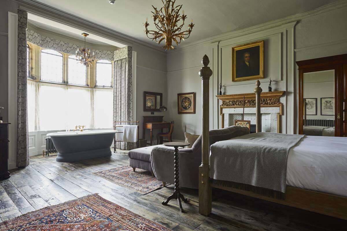 Um quarto tradicional com uma cama grande, uma banheira de patinhas e um lustre clássico.