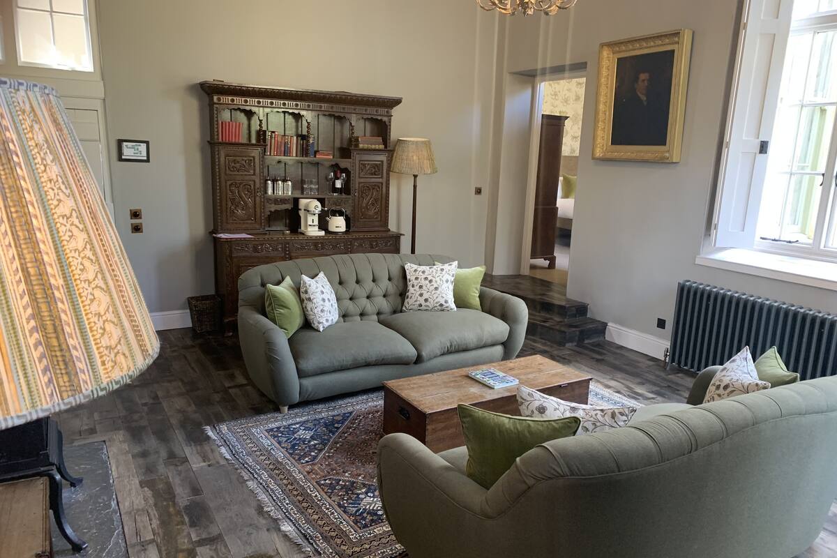 Uma sala de estar com um sofá verde, um armário de madeira, um tapete estampado e uma luminária.