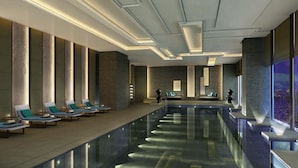 Piscina interior moderna com espreguiçadeiras, vista para a cidade e iluminação contemporânea.