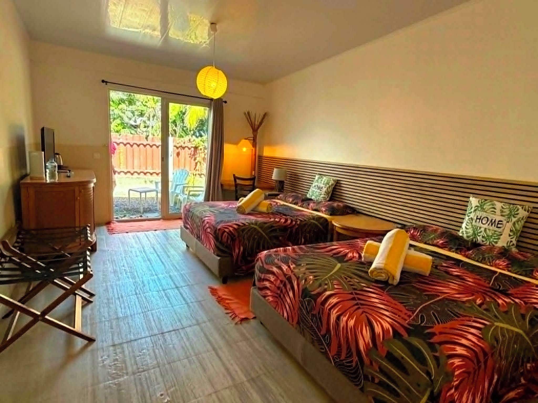 Quarto de hotel com duas camas, uma escrivaninha, uma cadeira e vista para o exterior.