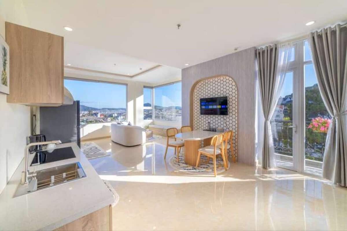 Cozinha moderna com fogão embutido, área de jantar com mesa redonda e cadeiras, e uma grande janela com vista para a cidade.