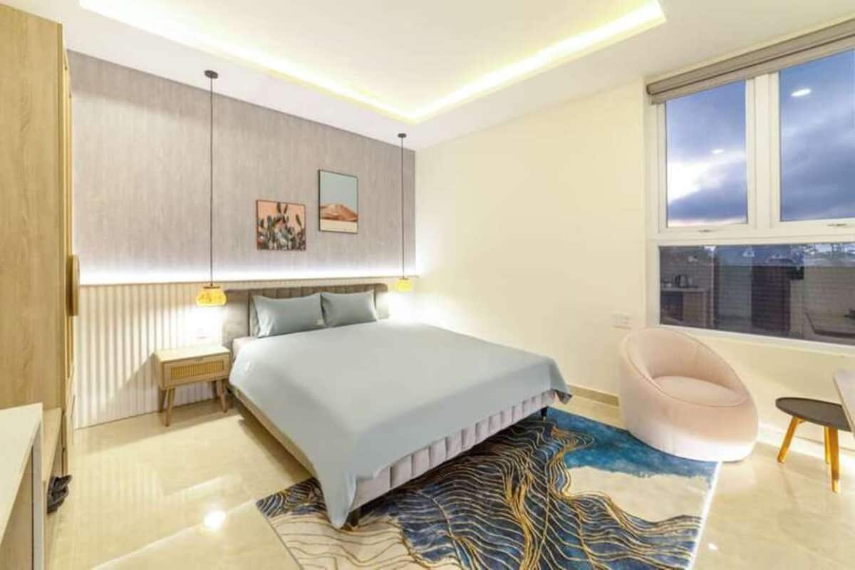 Quarto moderno com cama, mesas de cabeceira, uma cadeira e uma janela grande.