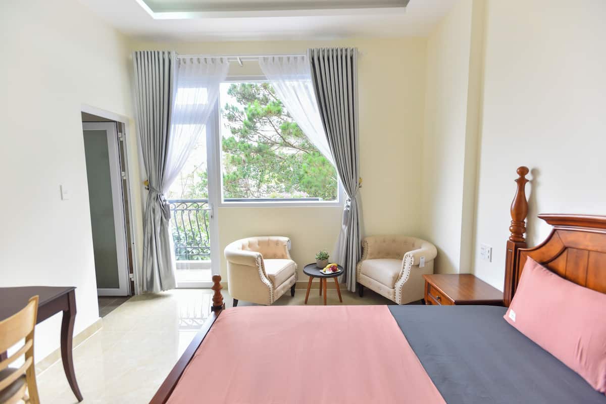 Quarto com cama, duas poltronas, uma mesinha com uma planta e uma mesinha de cabeceira.