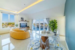 Uma sala de estar moderna com uma mesa redonda, cadeiras transparentes, um sofá amarelo e uma televisão.