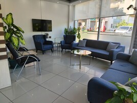 Um saguão de hotel moderno com um sofá, cadeiras, uma mesa de centro e grandes janelas com vista para a rua.