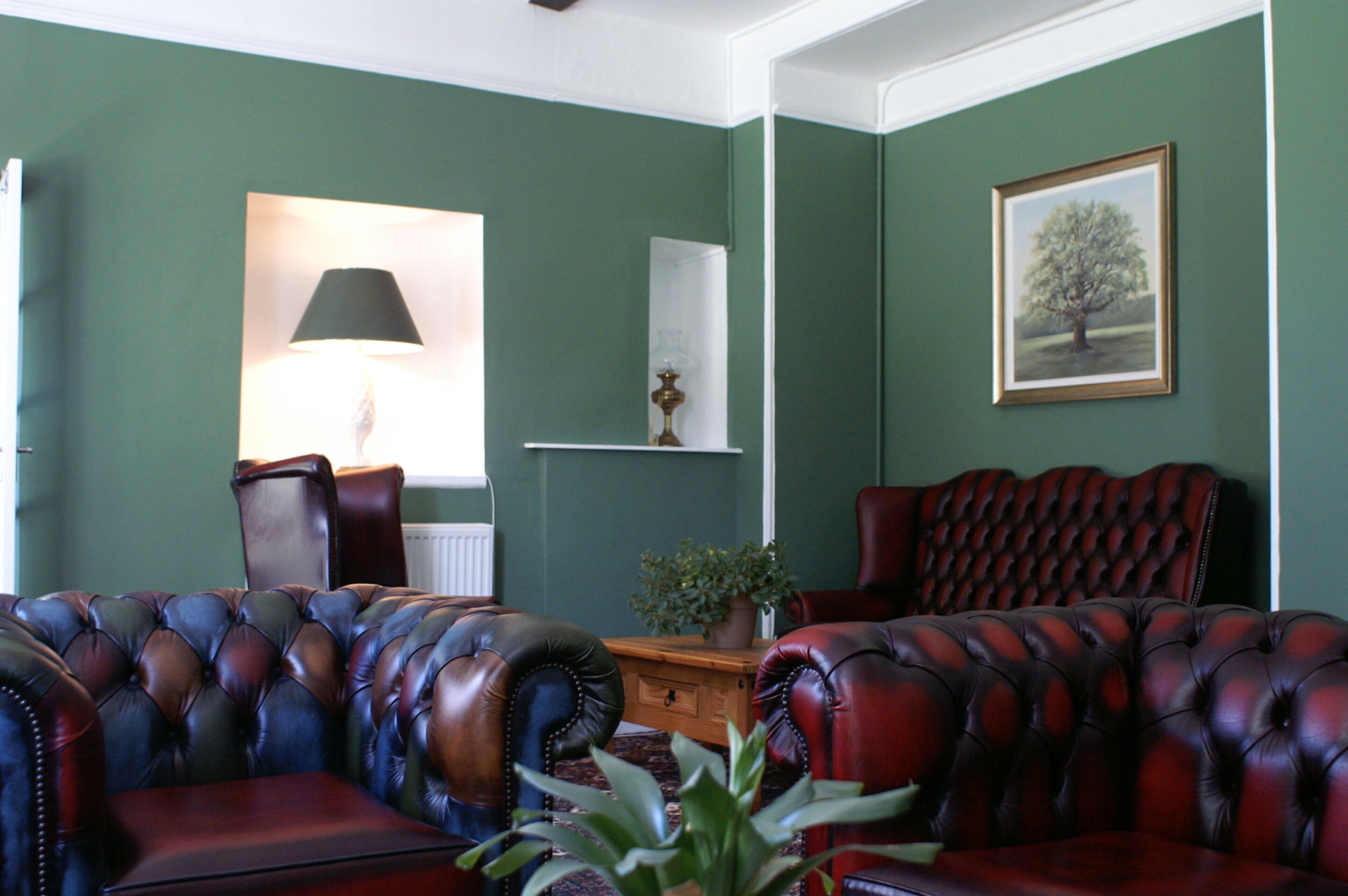 Quarto com paredes verdes, uma luminária, um quadro emoldurado e poltronas de couro.