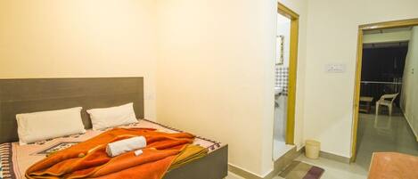 Quarto de hotel com uma cama, uma mesinha, uma cadeira e uma porta que dá para outro cômodo.