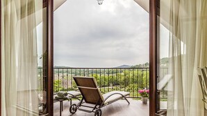 Varanda com cadeira e mesa, com vista para um jardim e colinas ao longe.