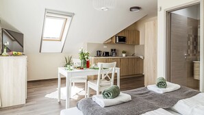 Quarto moderno com uma cama grande, uma escrivaninha e uma kitchenette ao fundo.