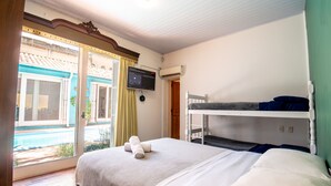 Quarto de hotel com uma cama, televisão, janela com cortinas e vista para um edifício.