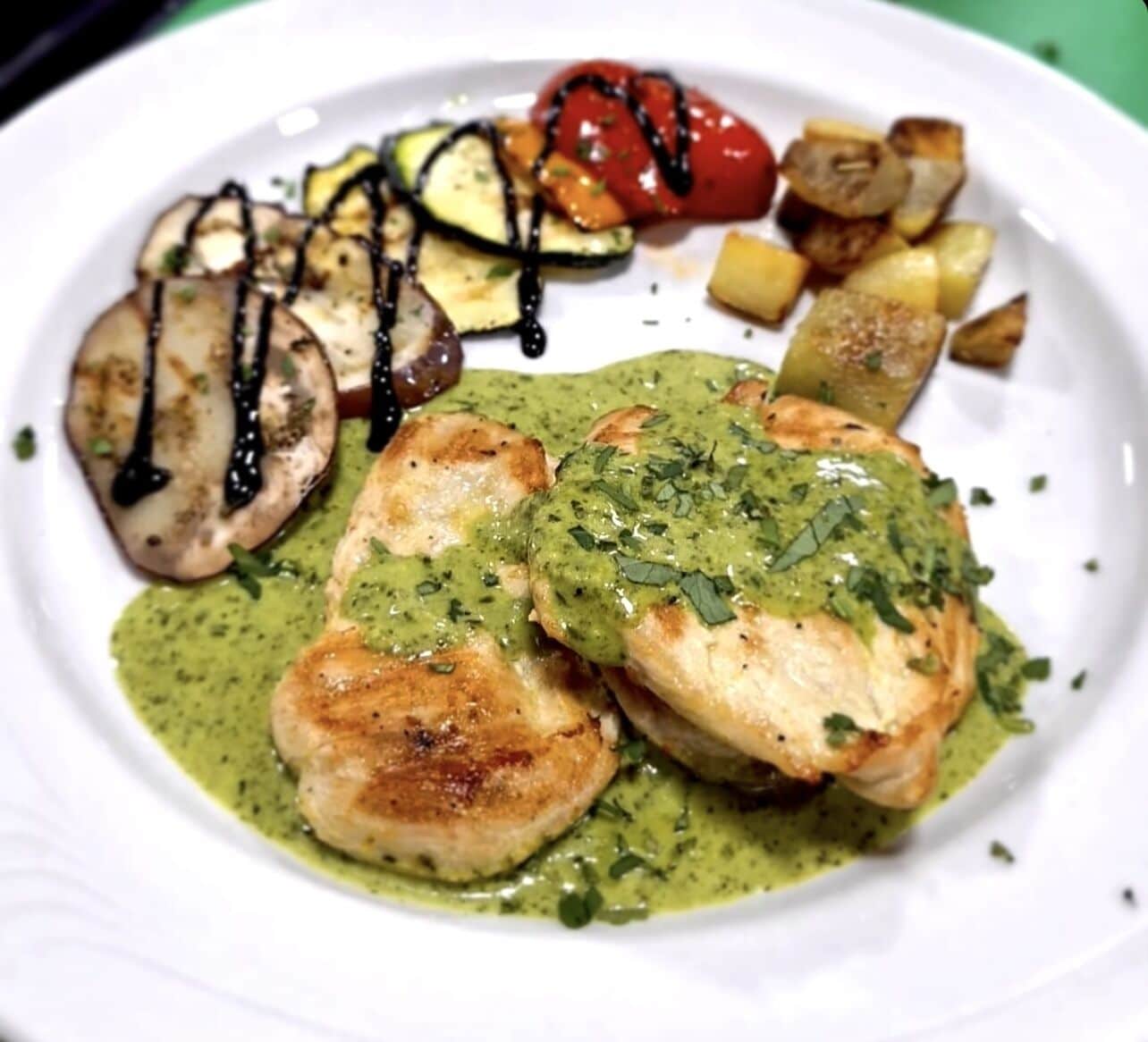Prato de comida com frango, legumes e um molho verde.