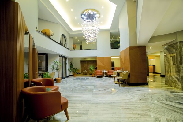 Um hall amplo com teto alto, um candelabro, áreas de estar e piso de mármore polido.