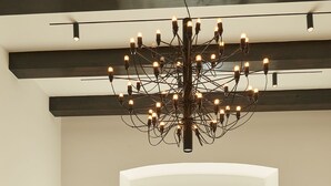 Uma sala de jantar com um lustre, mesas redondas e cadeiras.