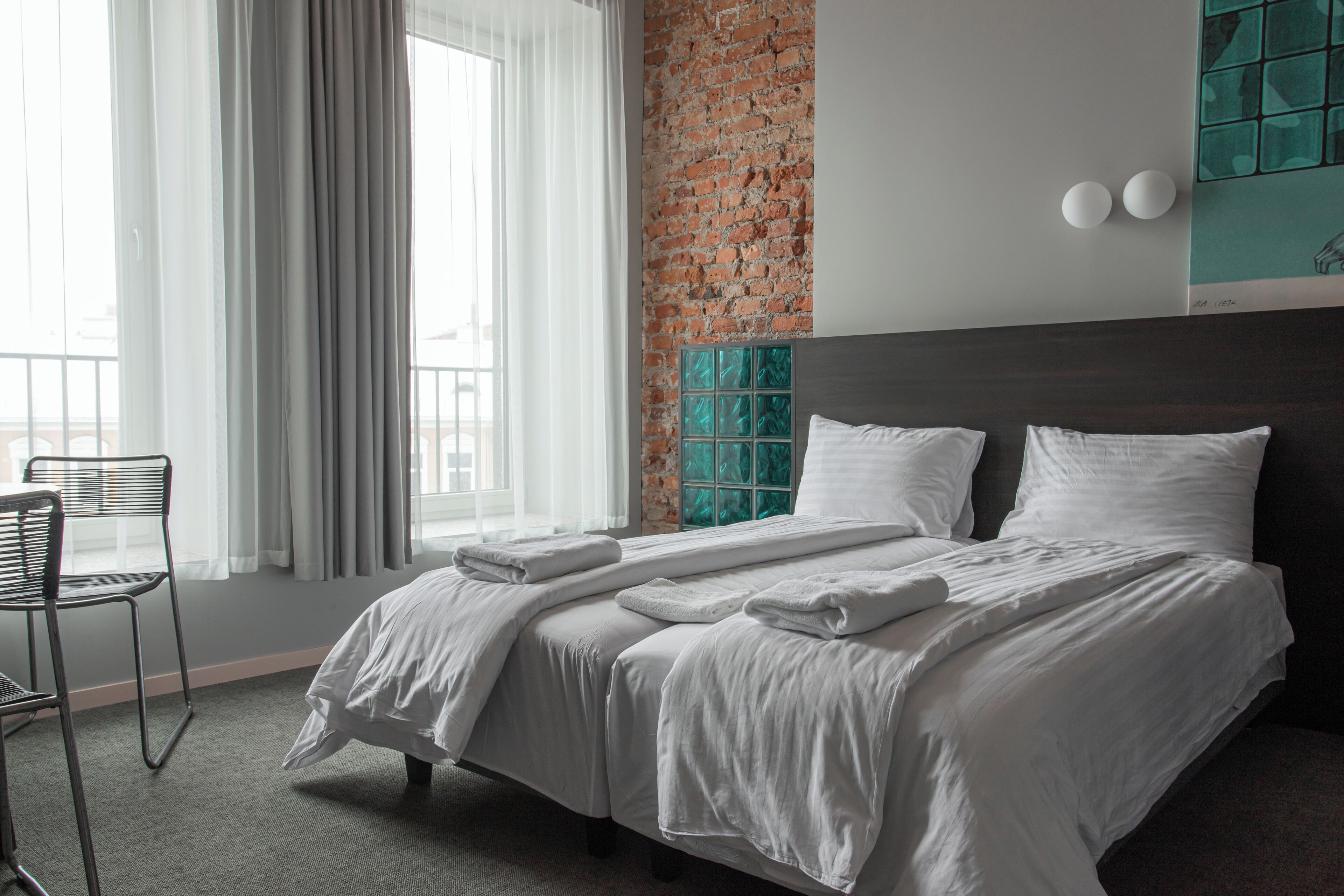 Quarto de hotel com uma cama grande, uma cadeira, uma parede de tijolos e uma janela com cortinas.
