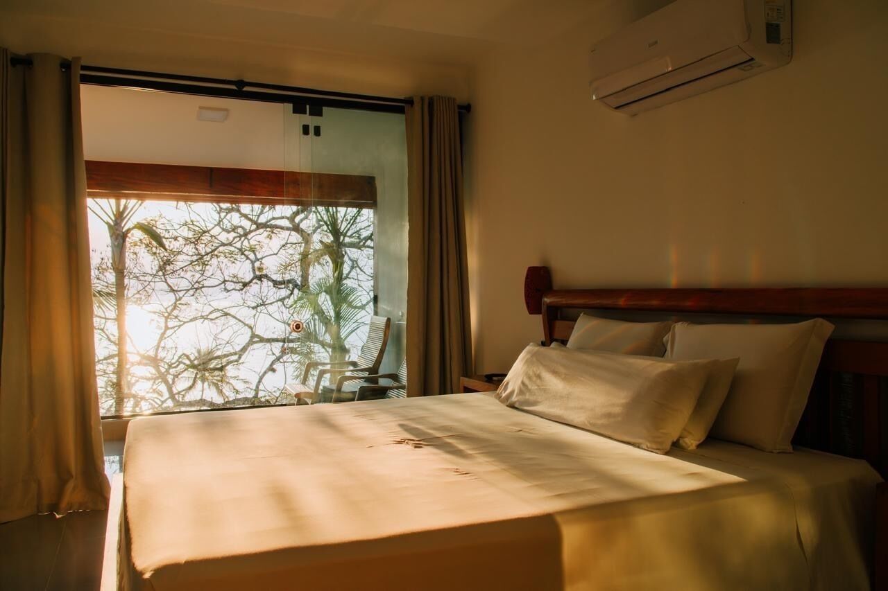 Quarto de hotel com cama, janela com cortinas e aparelho de ar condicionado na parede.