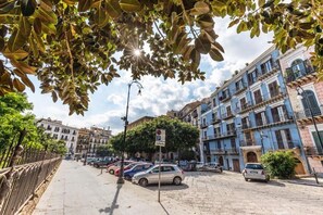 Uma rua com carros estacionados, edifícios com varandas e céu claro.