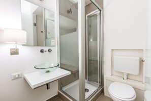 Um banheiro moderno com pia de vidro, vaso sanitário e chuveiro sem barreiras.