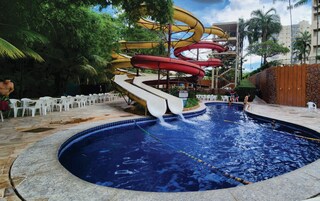 Piscina com vários toboáguas, cercada por palmeiras e um muro de pedra.
