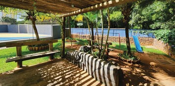 Uma área externa coberta com piscina, bancos de madeira e um parquinho.