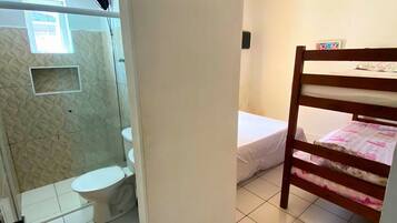 Quarto pequeno e limpo, com chuveiro, sanitário e uma cama.