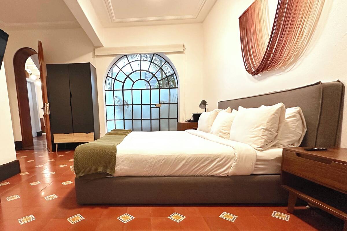 Quarto com uma cama grande, uma mesa de cabeceira, uma janela com vista e uma porta que dá para outro espaço.
