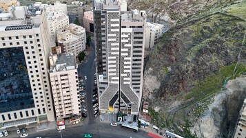 Um edifício alto com fachada geométrica peculiar, rodeado por outros edifícios e uma encosta íngreme.