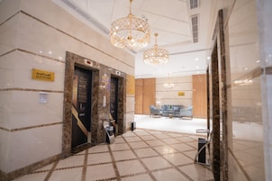 Um saguão de hotel com piso de mármore, dois elevadores, uma recepção e lustres.