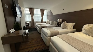 Quarto de hotel com duas camas, uma escrivaninha, televisão e um pequeno espaço de estar com cortinas.
