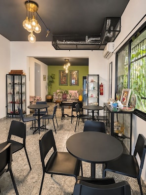 Um interior moderno com área de estar, mesas e cadeiras, destacando uma parede verde e uma janela grande com plantas.