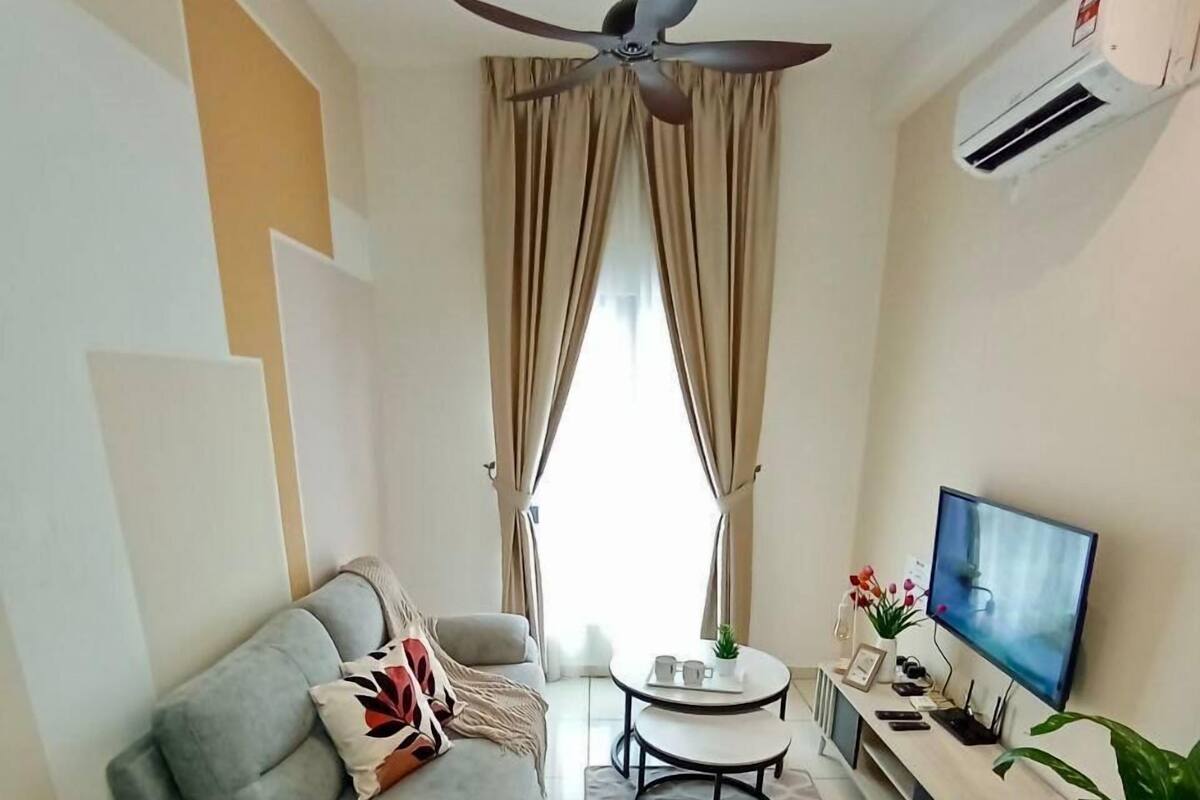 Uma sala de estar com um sofá cinzento, uma mesa de centro, uma televisão e um ventilador de teto.